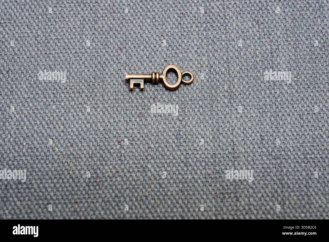 A tiny key sits alone on flat gray surface with a faint worn shine on ...