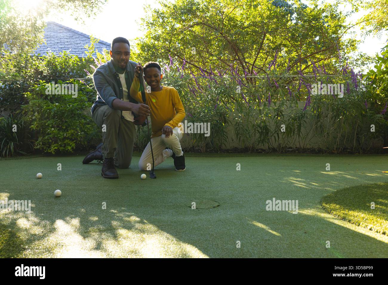 Father and African American son playing mini golf on outdoor course ...