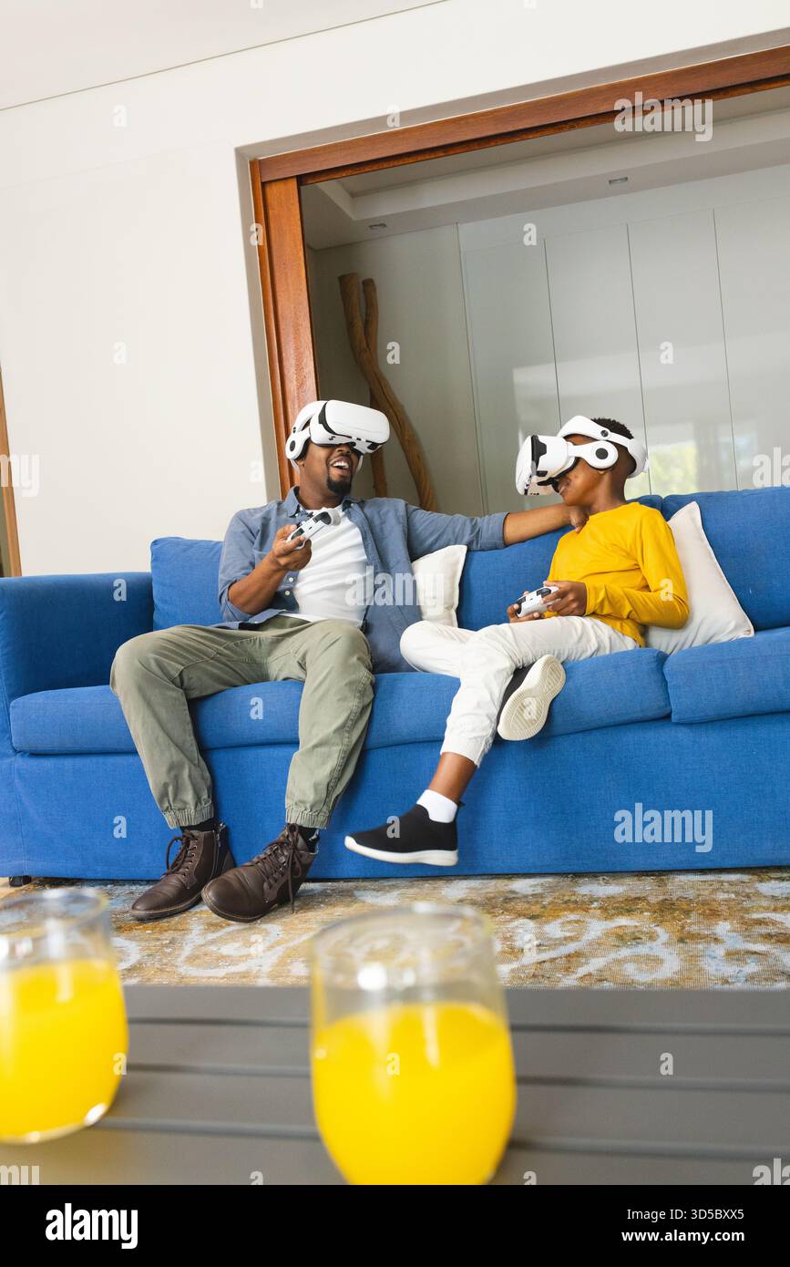 Father and son enjoying virtual reality gaming together on blue sofa at ...