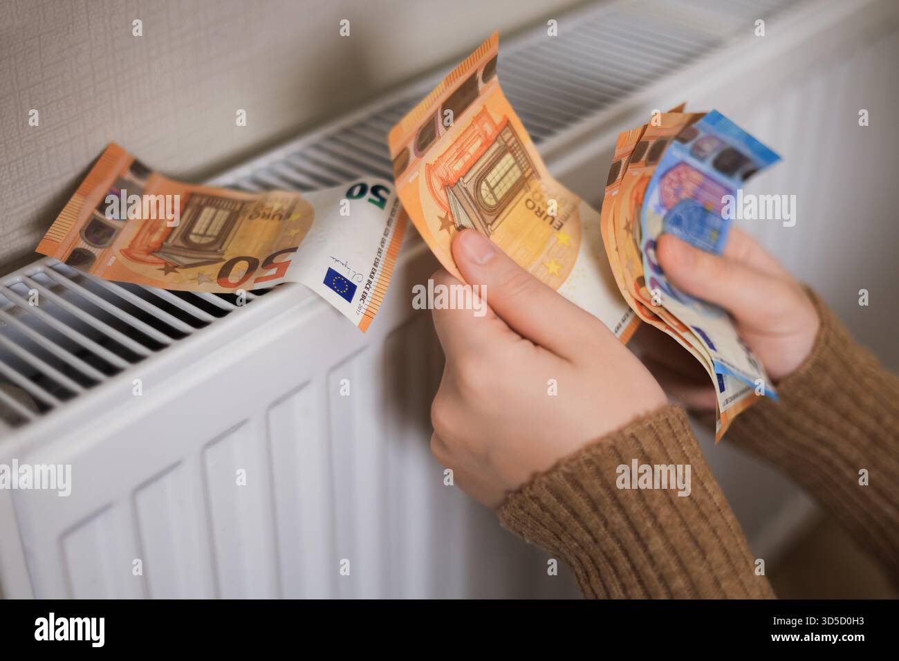 A girl in a sweater counts money by the radiator: euros in 50 and 20 ...
