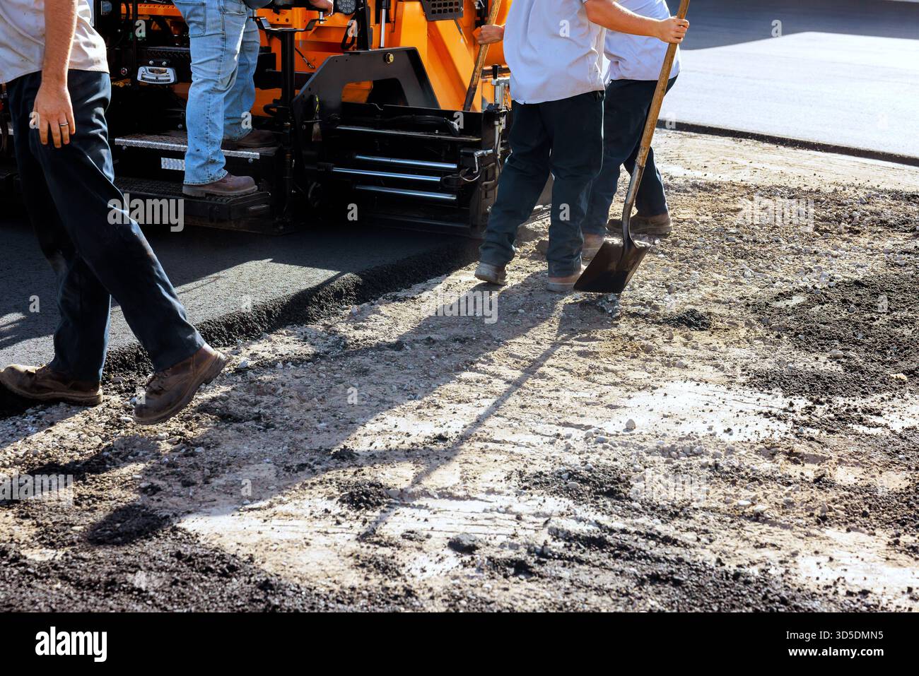 Construction workers lay asphalt using heavy machinery while others ...