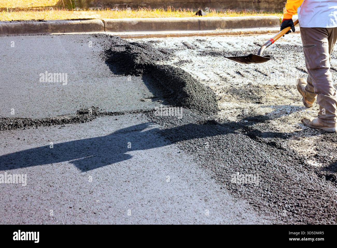 Construction worker spreads fresh asphalt on road under ensuring smooth ...