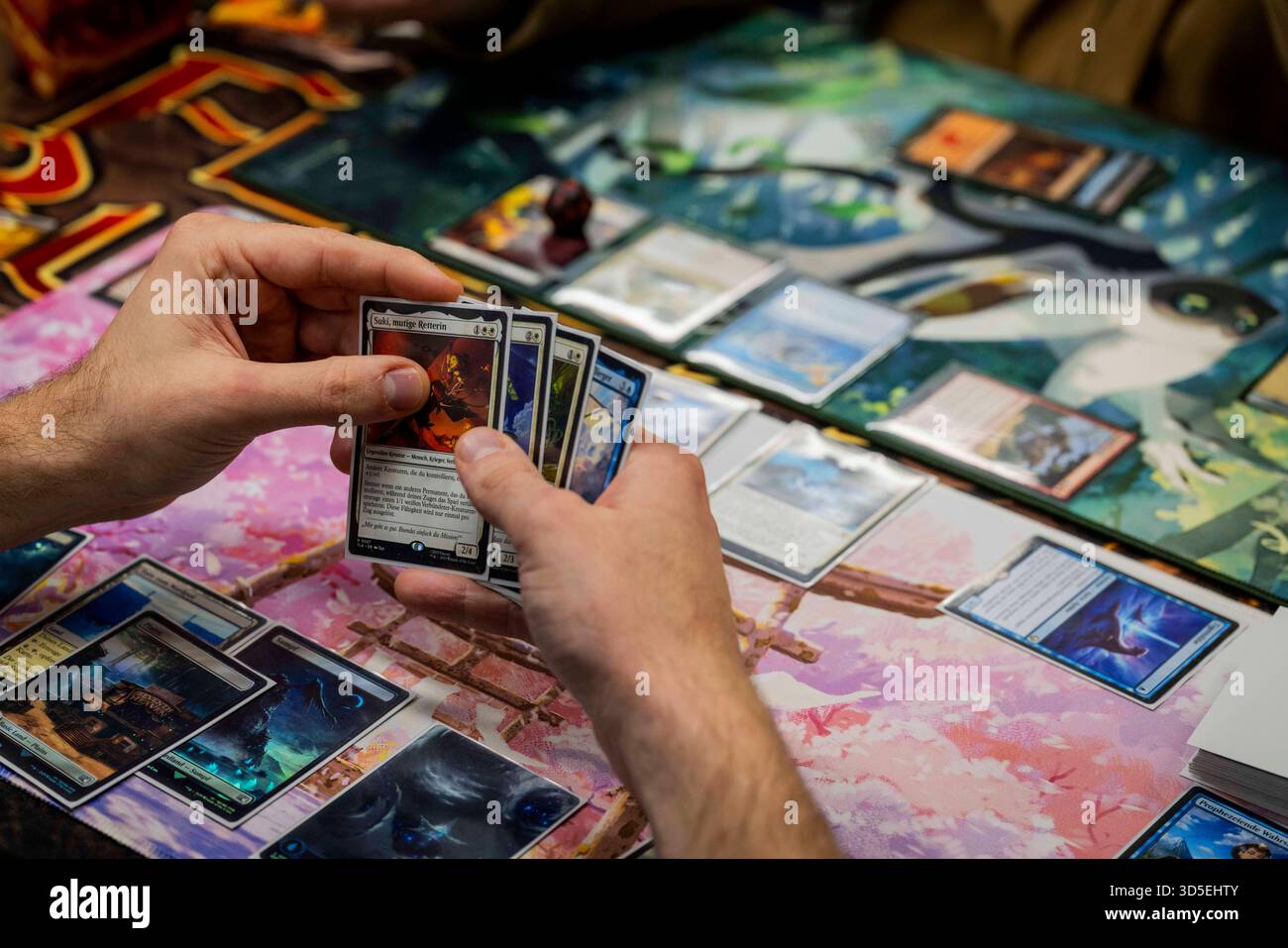 Hände halten Spielkarten. Im Hintgrund liegen Karten auf einer ...