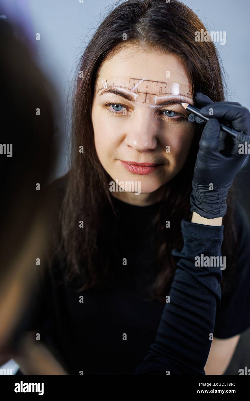 A permanent makeup artist marks a woman's eyebrows with a pencil ...