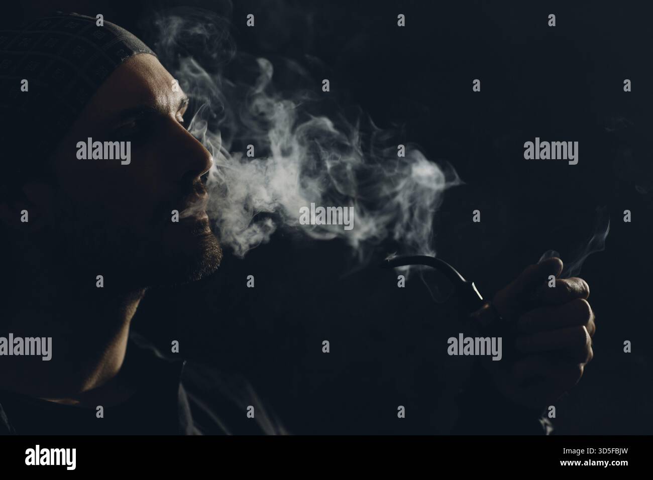 Man smokes smoking pipe against dark background. Back side lit profile ...