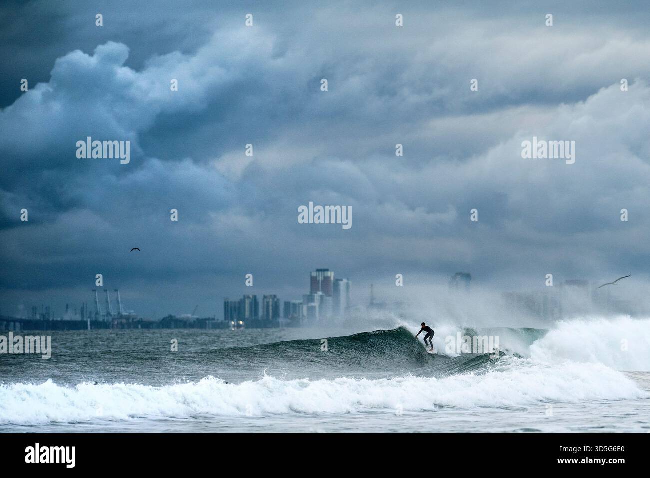 A surfer rides a wave as clouds gather above Bolsa Chica State Beach in ...