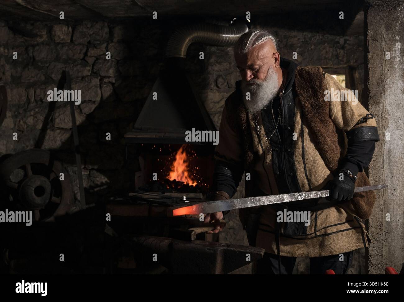 A Viking blacksmith with a white beard and braided hair works intently ...