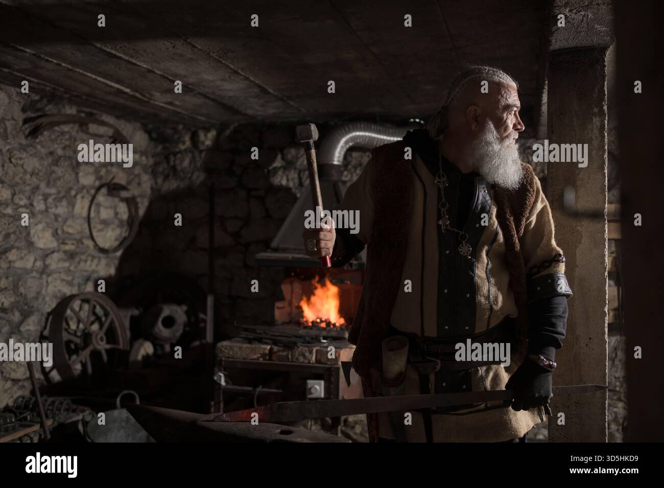 A Viking blacksmith with a white beard and braided hair works intently ...