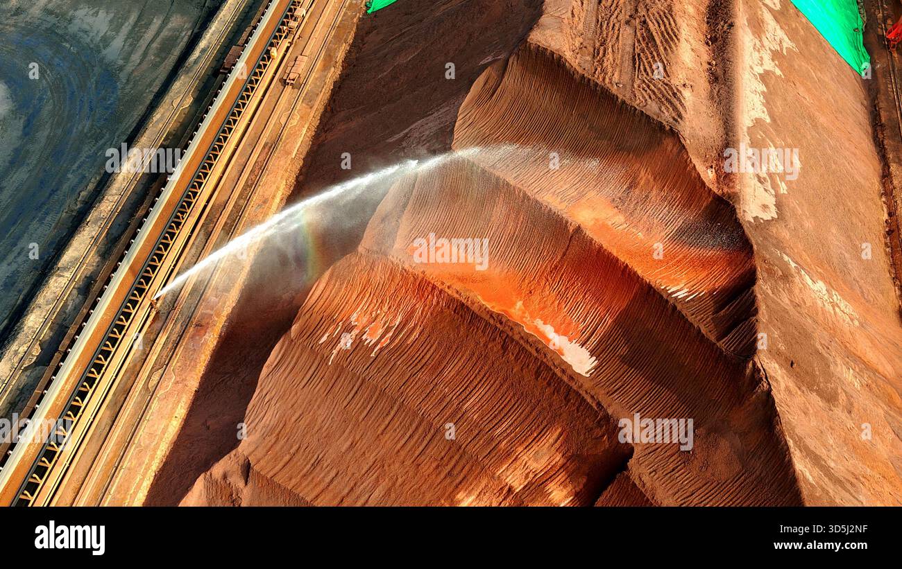 A nozzle sprays water on piles of iron ore to reduce dust at a port in ...
