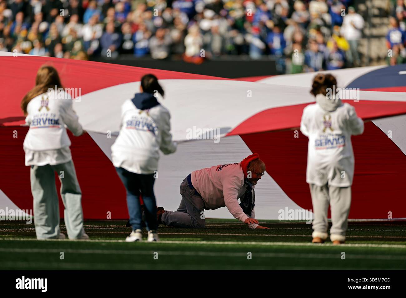 A volunteer crawls under a larger American flag before an NFL football ...