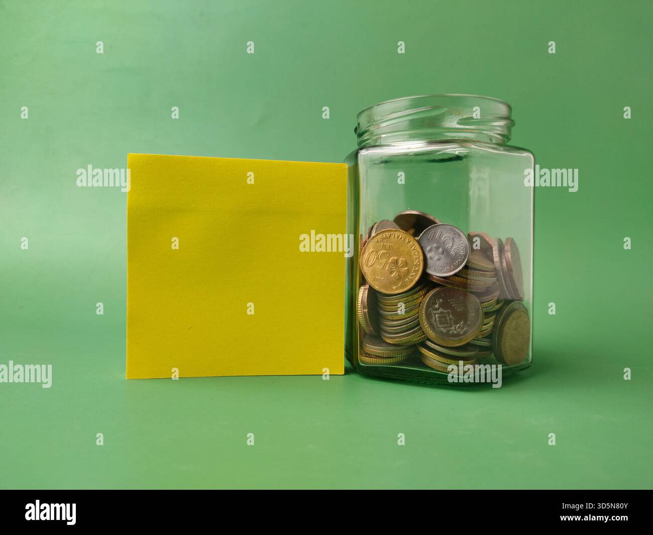 The image displays a glass jar filled with assorted coins and a blank ...
