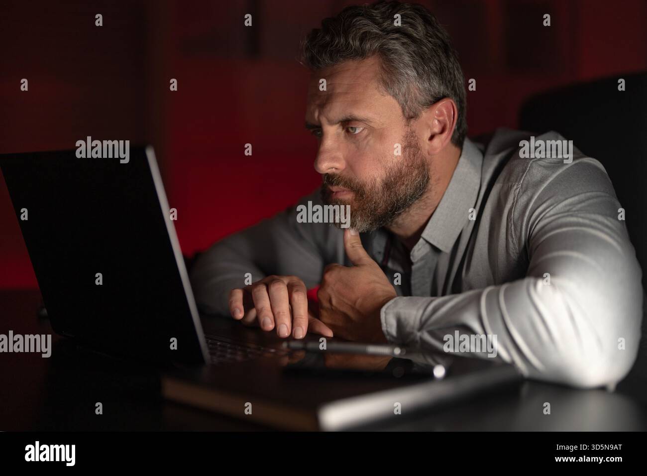 Tired businessman working late at night on a laptop in a dark office ...