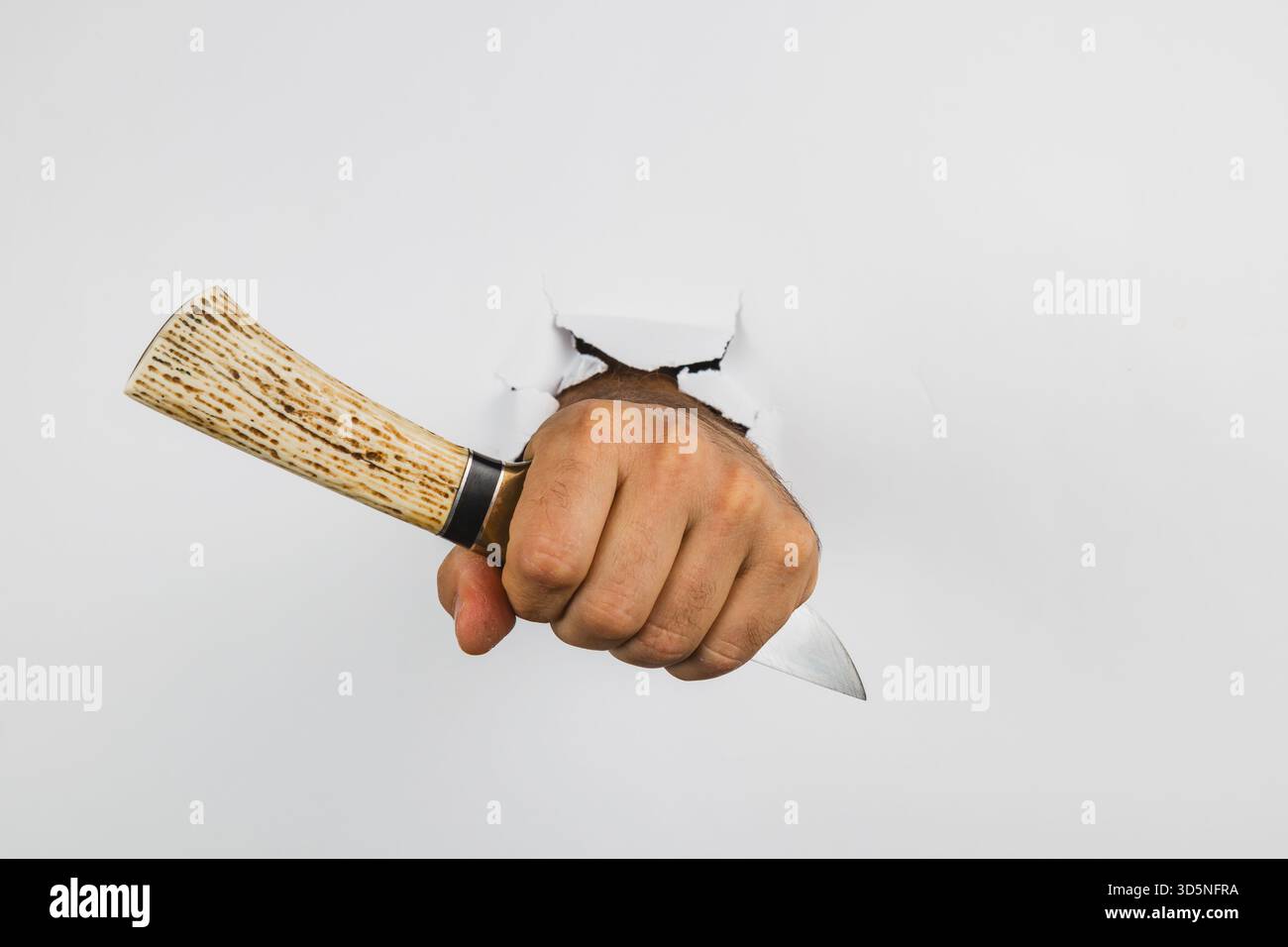 A strong hand grips a knife, pushing through a torn section of a white ...
