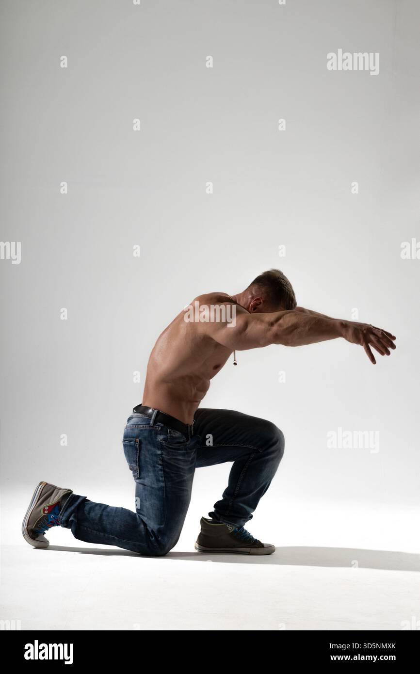 An athletic man showcases his strength in a studio kneeling with arms ...