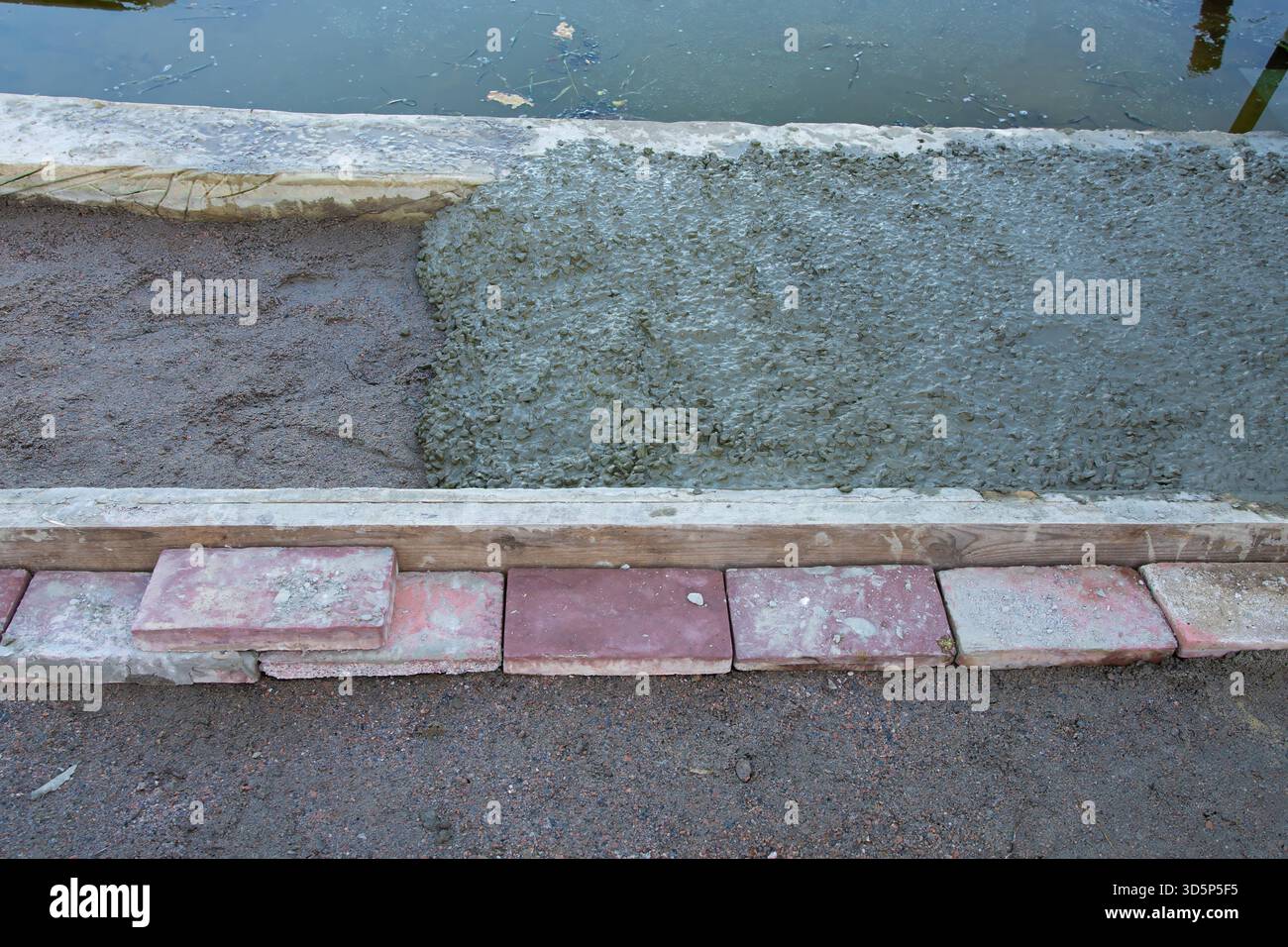 Fresh concrete poured into formwork next to sand base and paving bricks ...