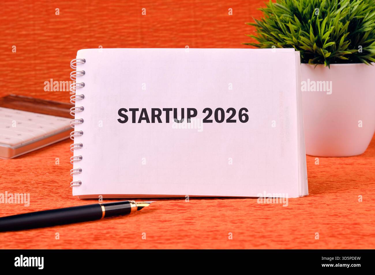 A notebook displays the words STARTUP 2026 next to a pen, desk calendar, and potted plant. The ...