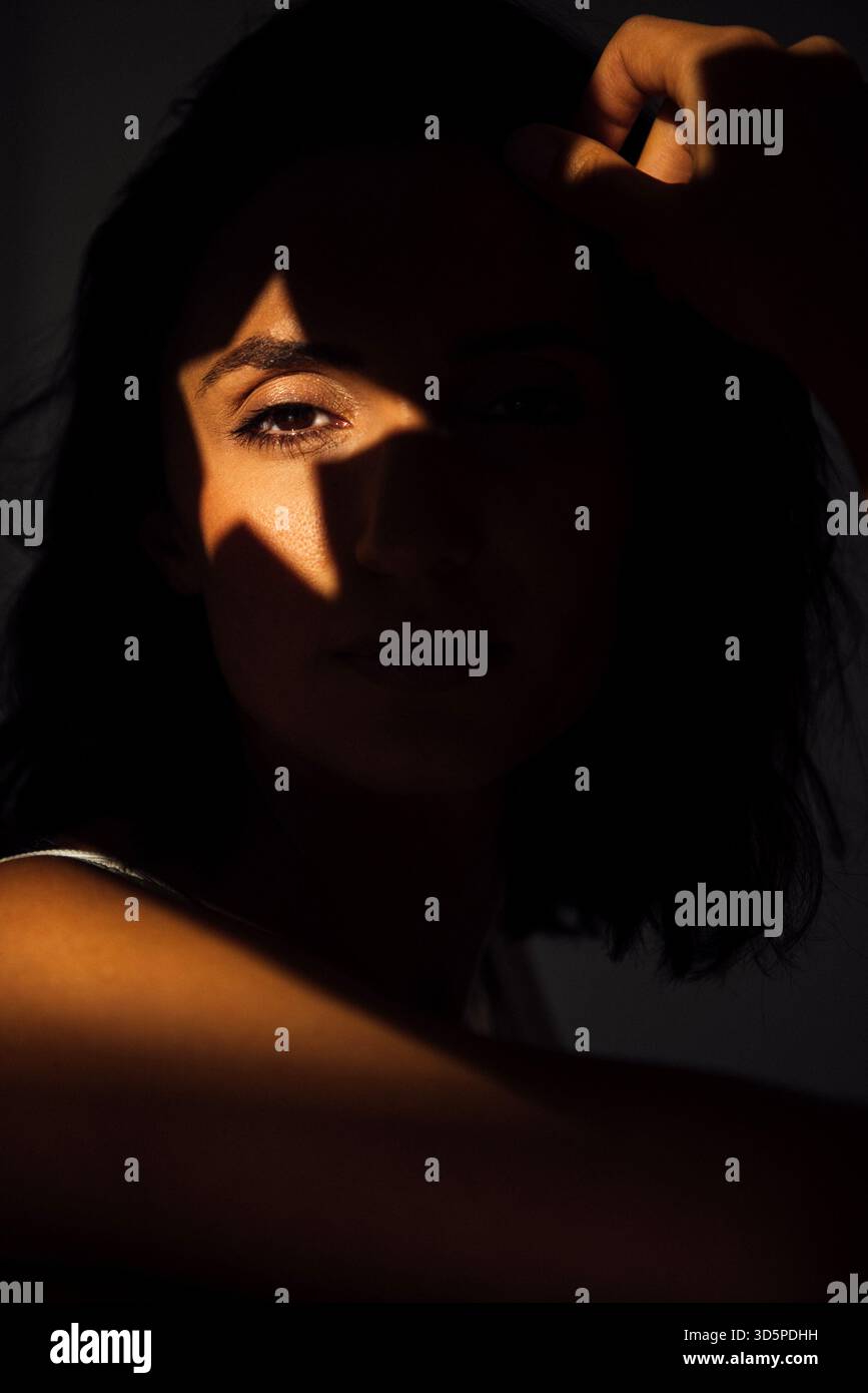 Female figure with dark hair is captured in striking light and shadow ...