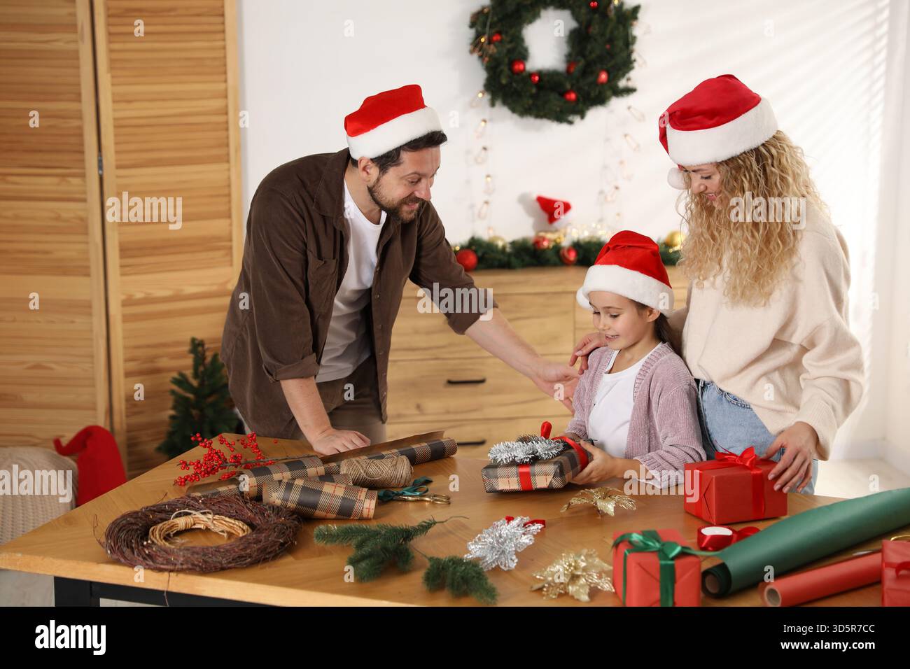 Happy family in Santa hats wrapping Christmas gifts at table indoors ...