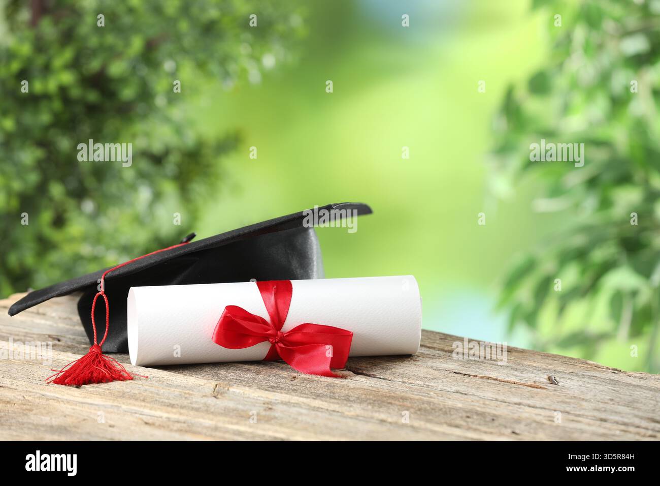 Graduation cap and diploma on wooden table against blurred background ...
