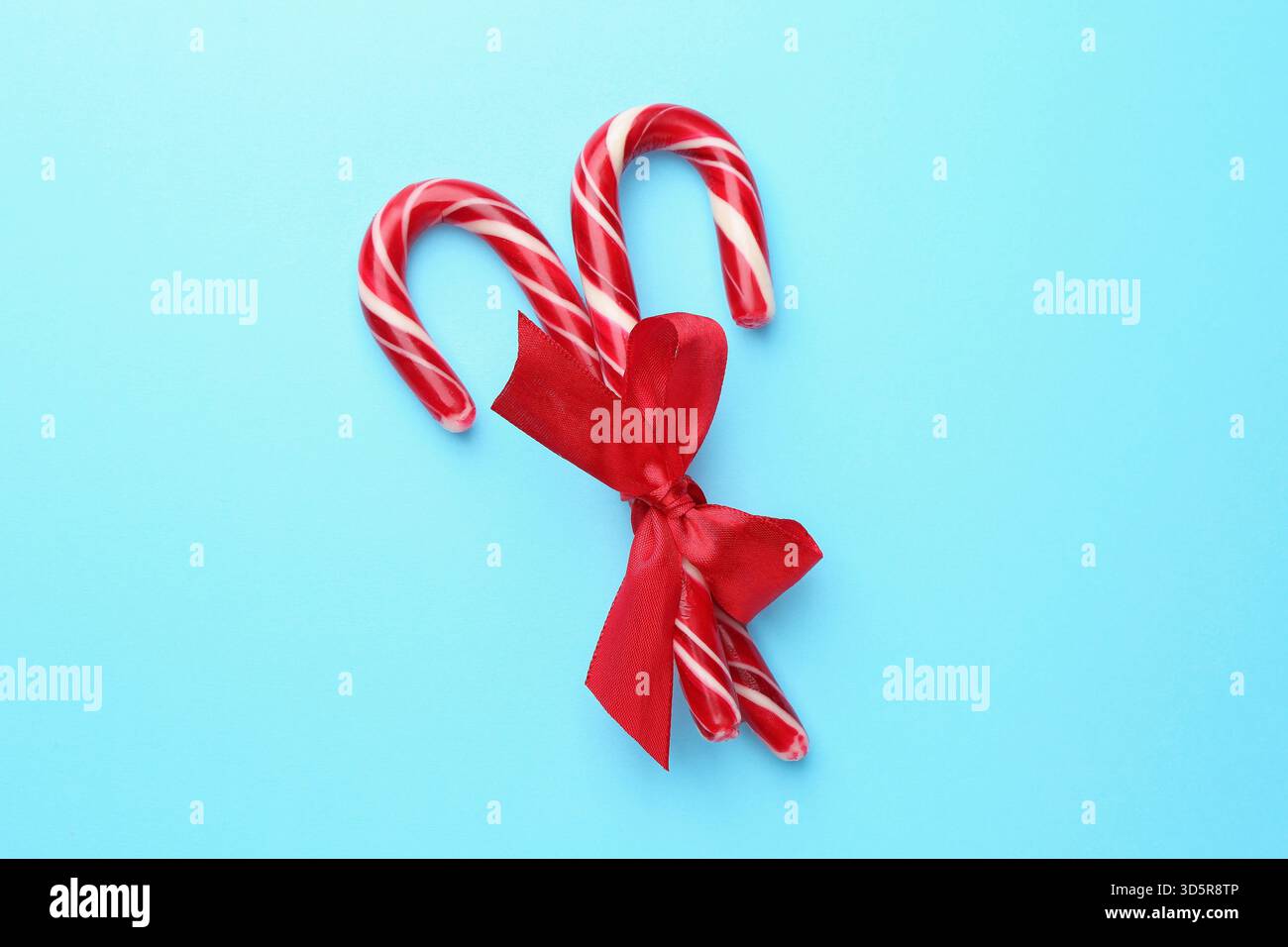 Tasty candy canes with bow on light blue background, top view. Merry ...