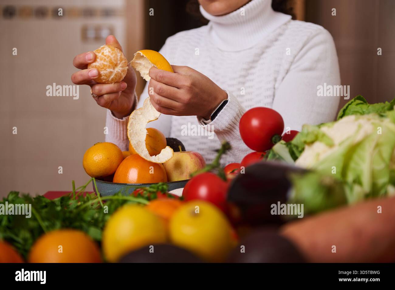 A person in a white turtleneck peels an orange amid a colorful spread ...
