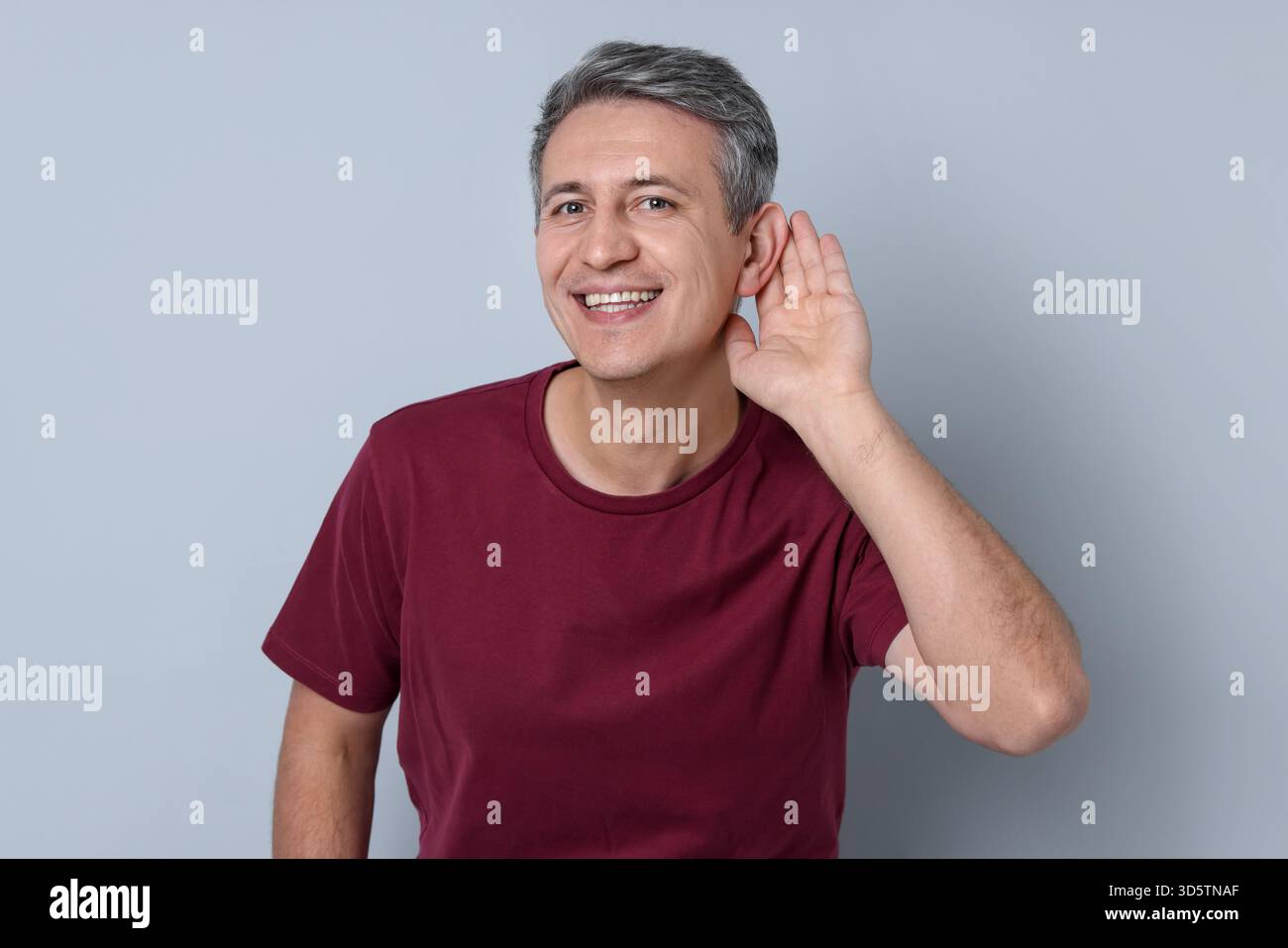 Man showing hand to ear gesture on light grey background Stock Photo ...