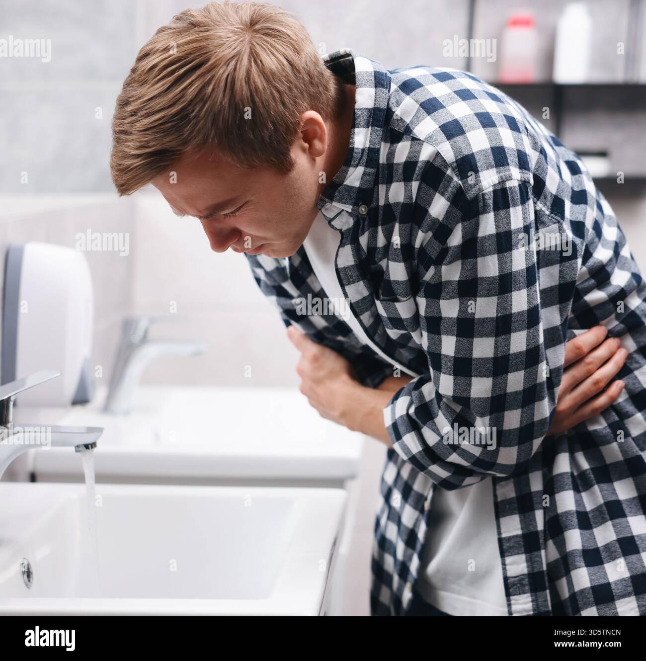 Young man suffering from nausea and stomachache over sink in bathroom ...