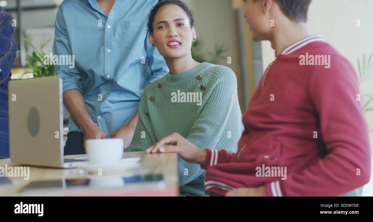 Speaking woman in mint-green sweater engaging colleagues at bright ...