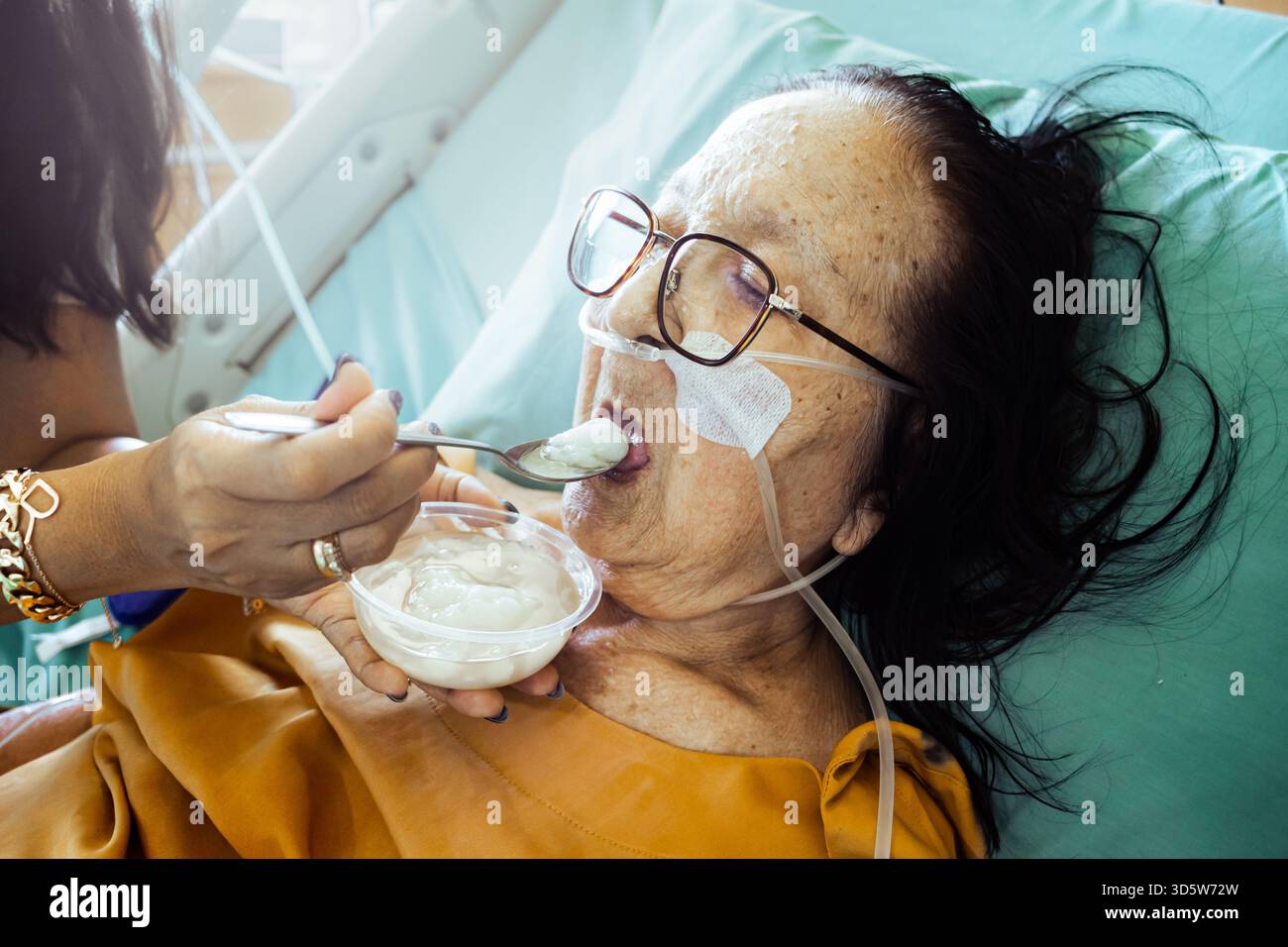 Sick Southeast Asian elderly female patient in hospital bed being feed ...