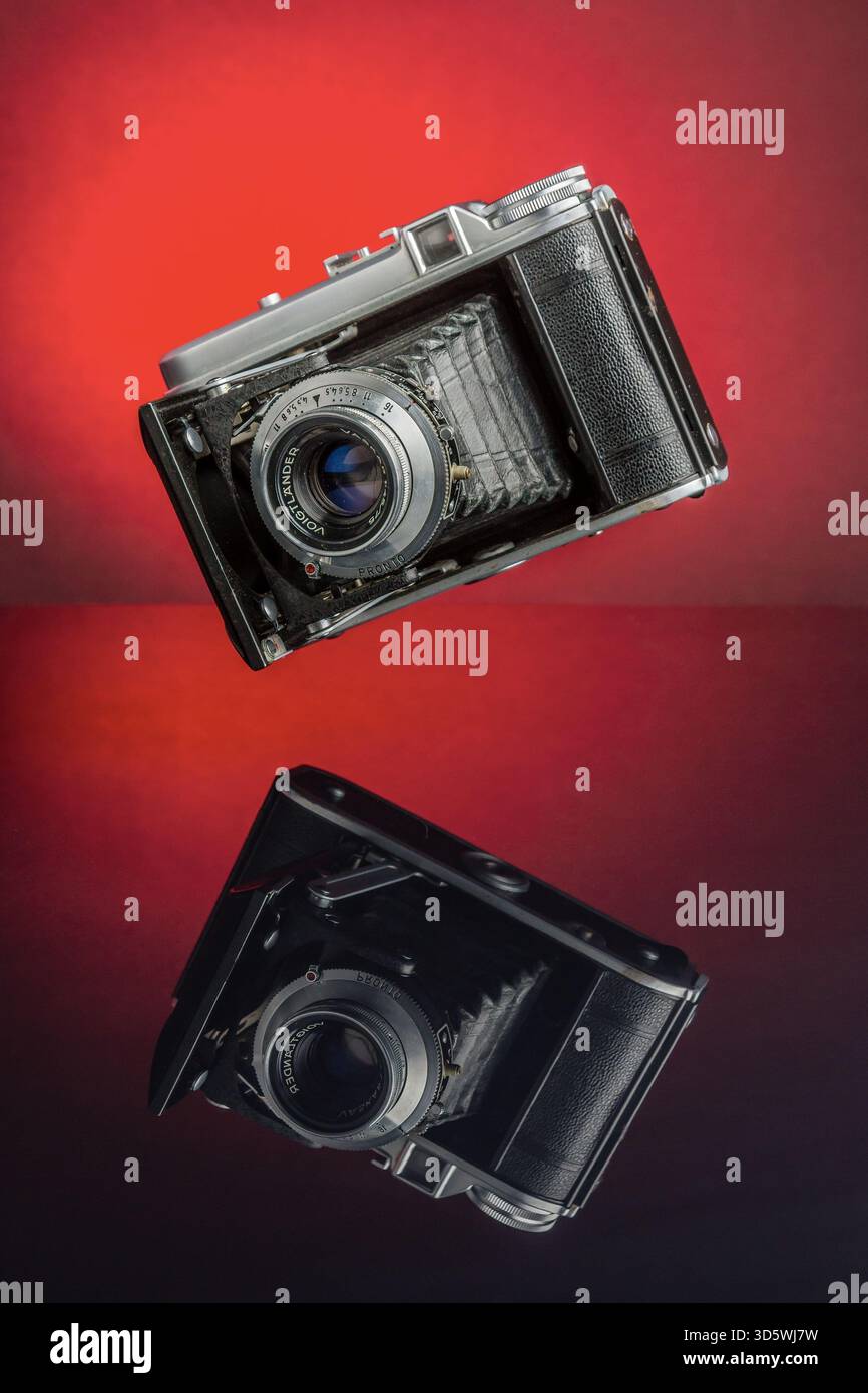 A vintage Voigtländer folding camera is suspended against a red ...