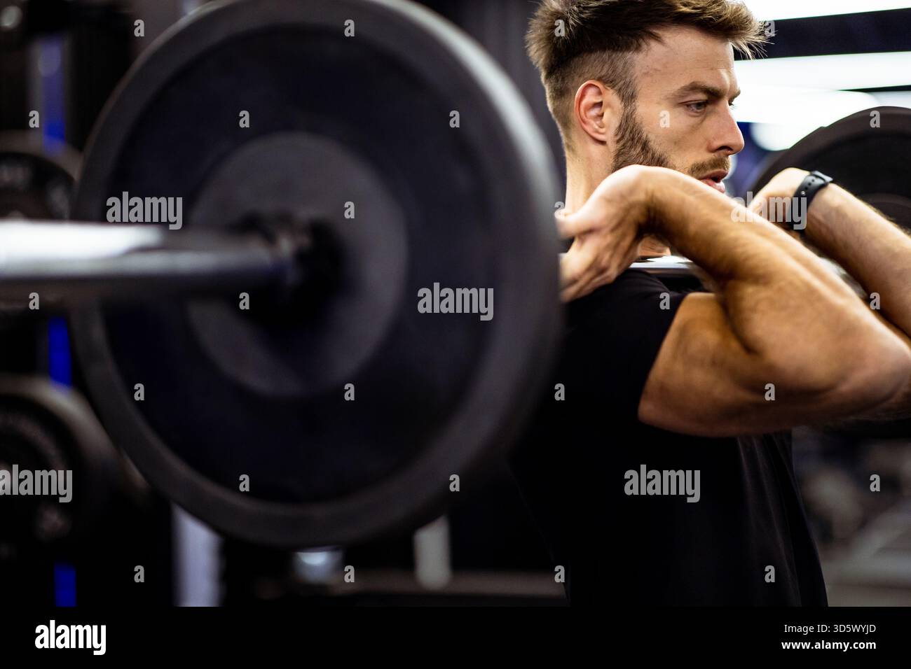 A man performs a weightlifting exercise in a modern gym. He focuses ...