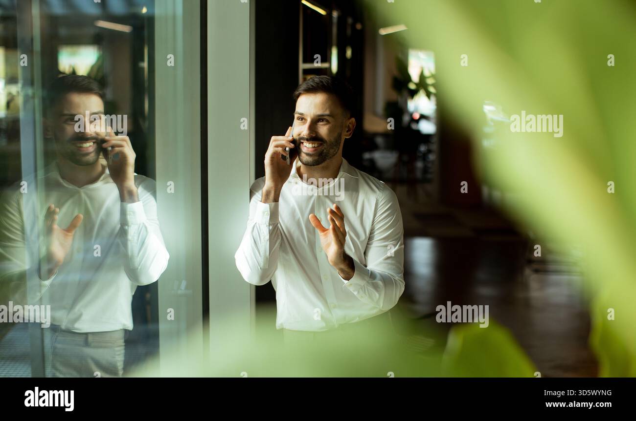 A man with a beard and white shirt stands by a window, smiling while ...