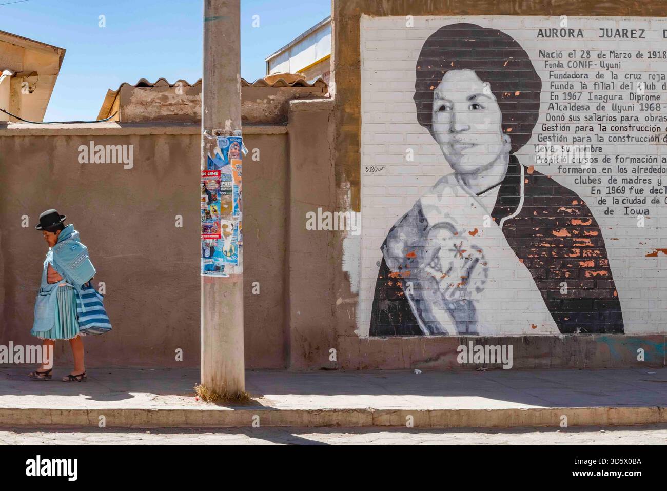 Indigenous Bolivian woman walking past a mural portraying a historic ...