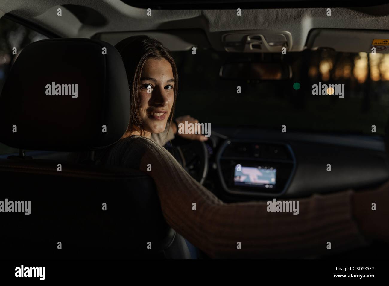 A young woman sitting in car and looking back in camera, over shoulder ...