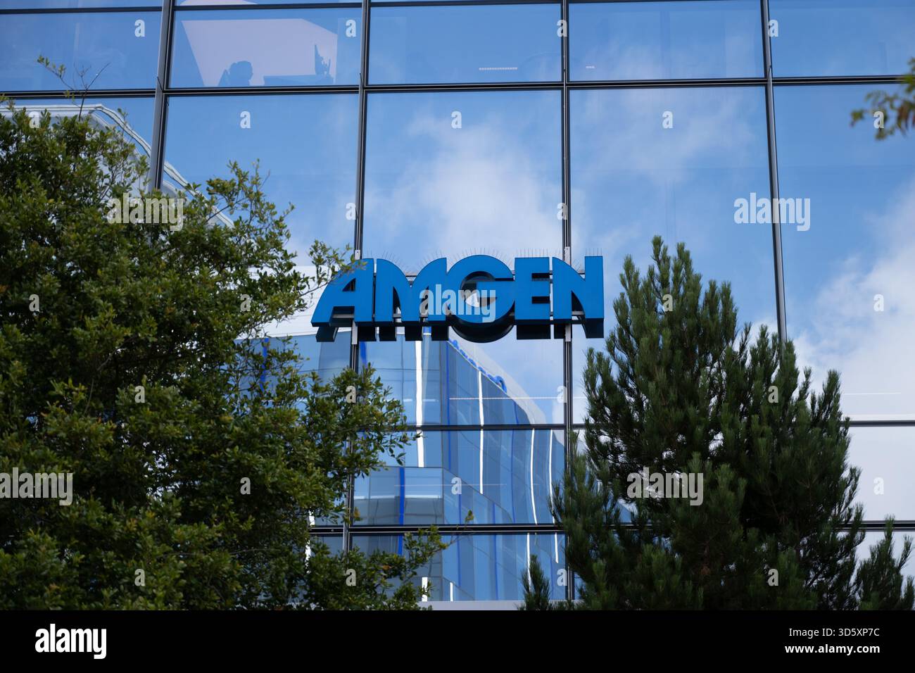 Amgen logo on glass facade of modern office building with trees and sky ...