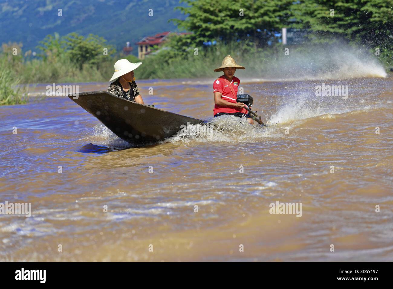 Two people ride in a small boat with big hats on a river, Inle Lake ...