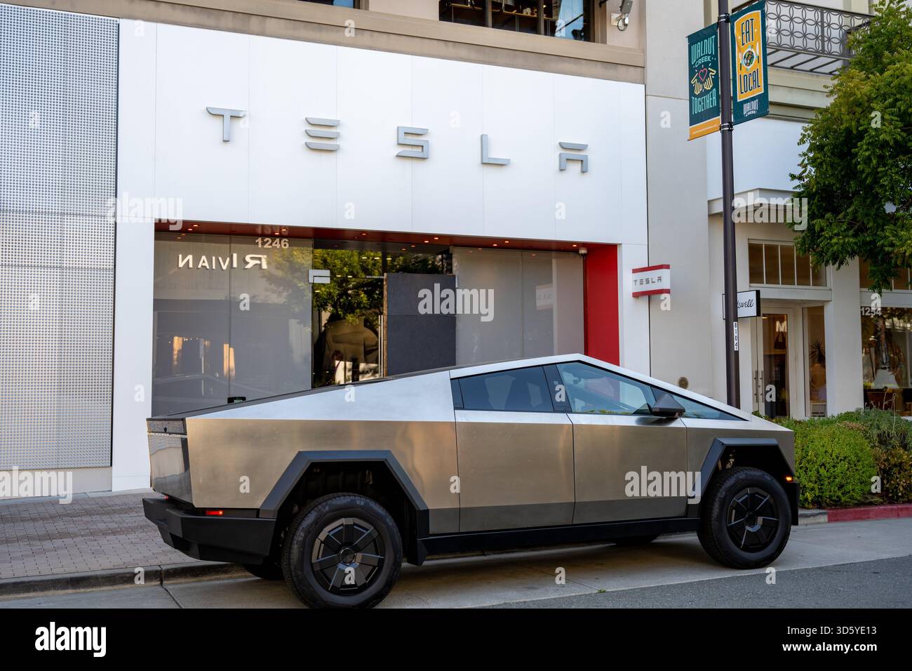 A Tesla Cybertruck is parked outside a Tesla store with signage and ...