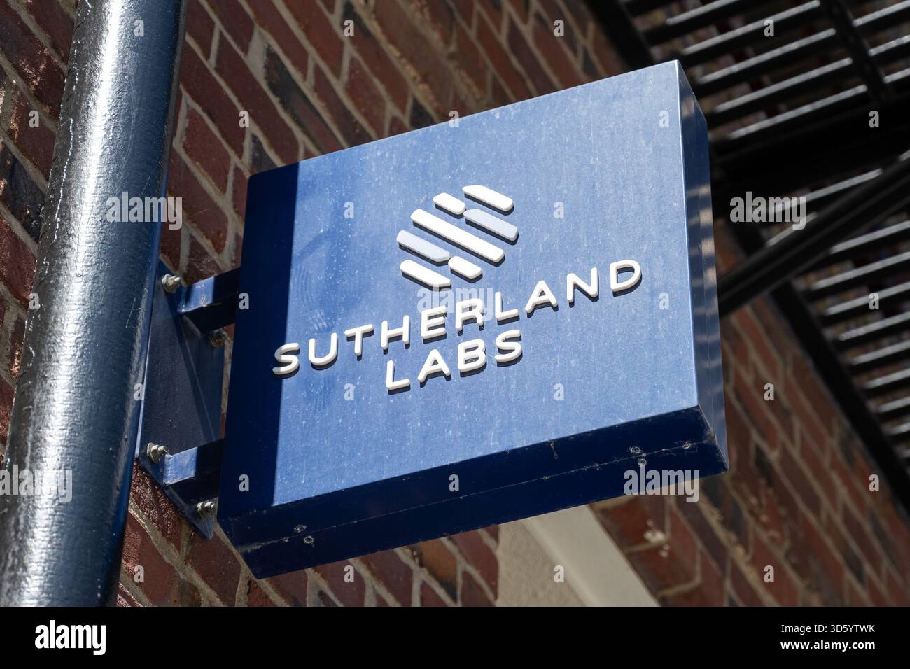Blue projecting sign for Sutherland Labs on brick facade with logo ...