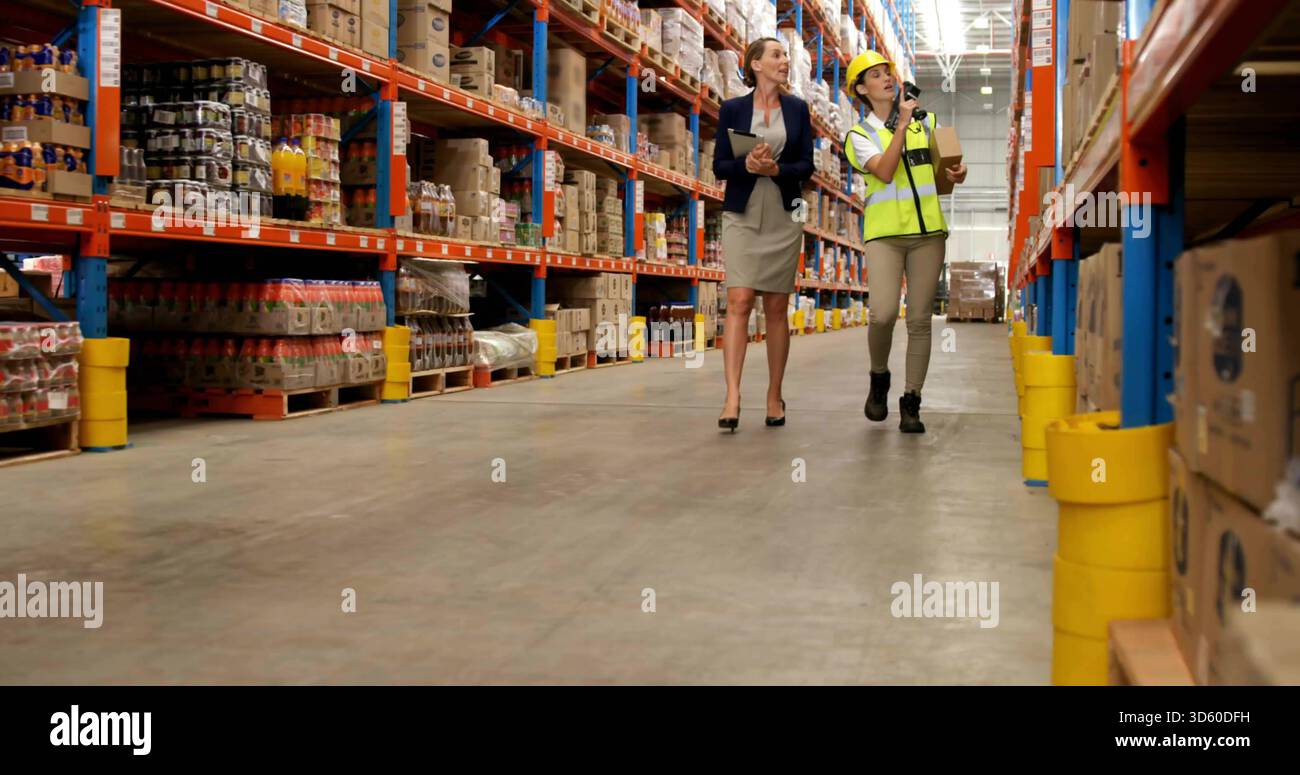 Walking two women in blazer, hard hat and vest, carrying tablet and ...