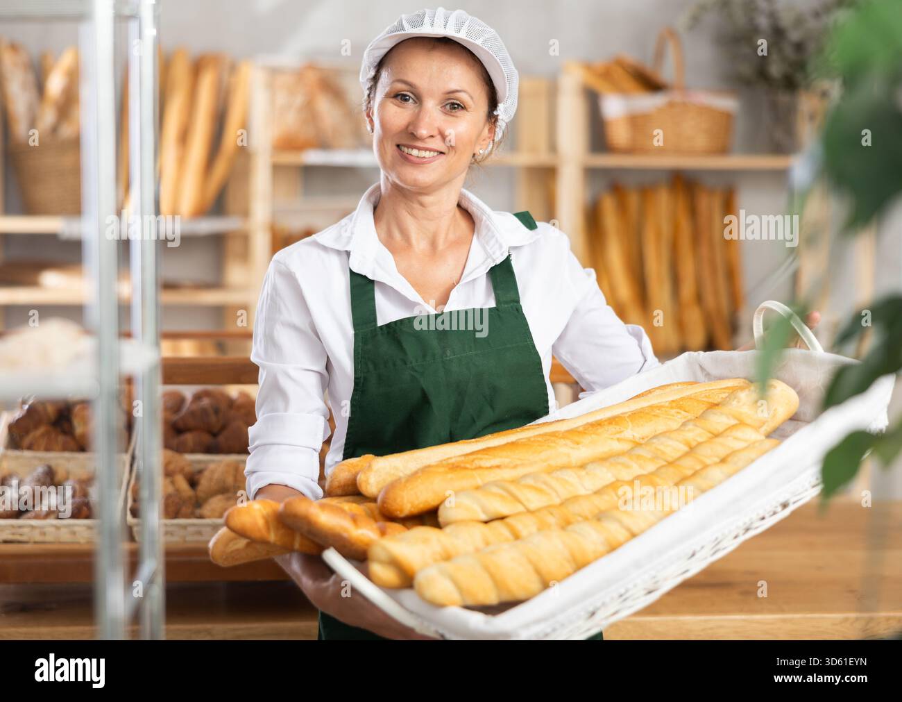 Female baker worker sells baguette, shows many products Stock Photo - Alamy