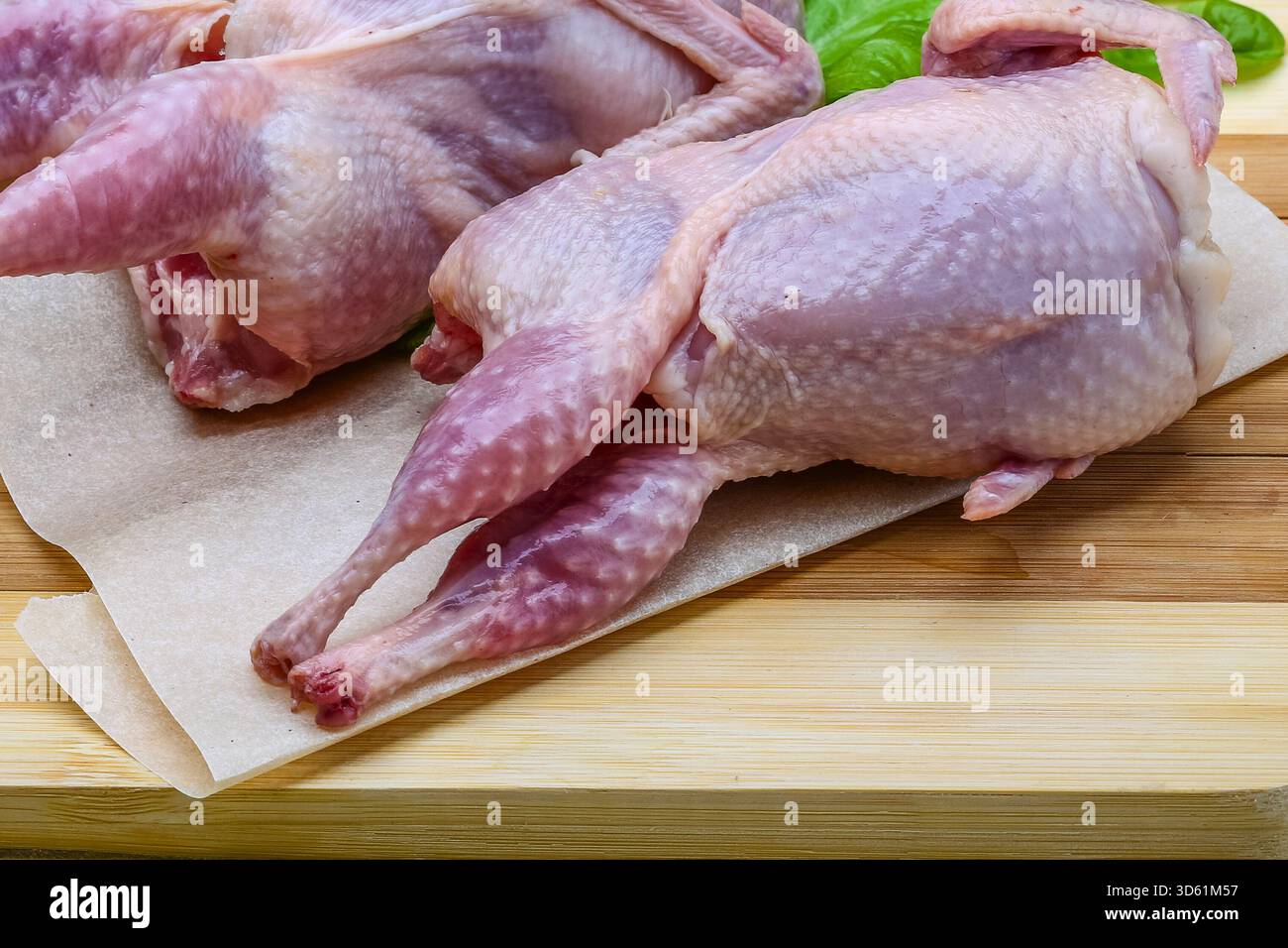 Two whole raw quail are presented on parchment paper atop a rustic ...