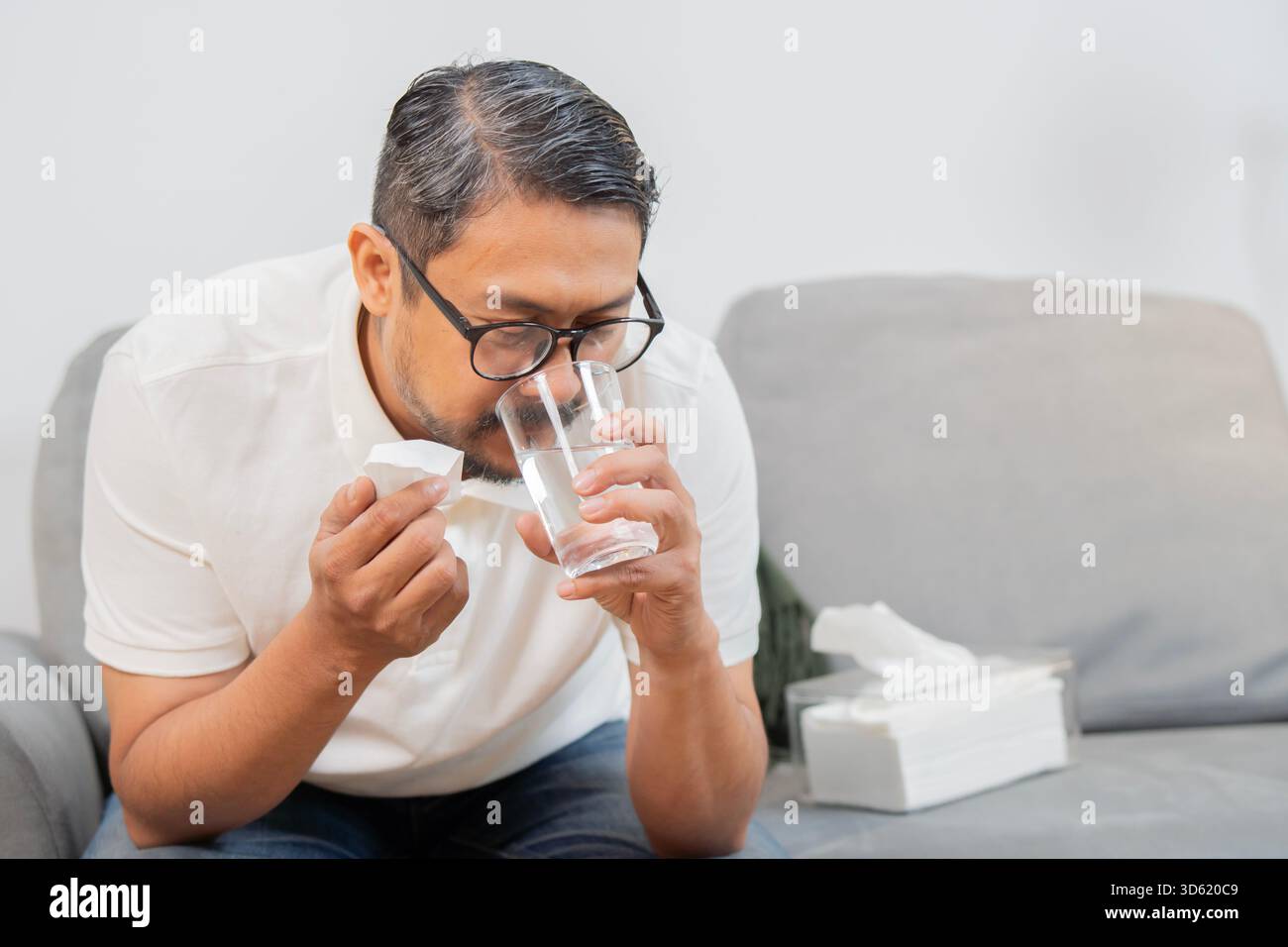 Sick man holding tissue and drinking water while coughing in the living ...