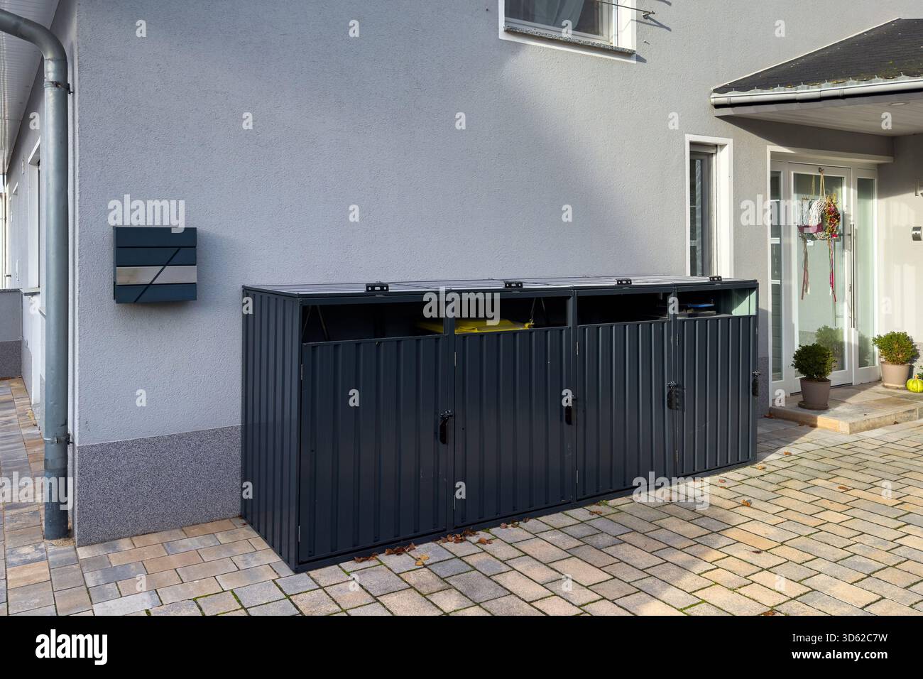 A sleek gray storage unit holds waste bins outside a modern home. The ...