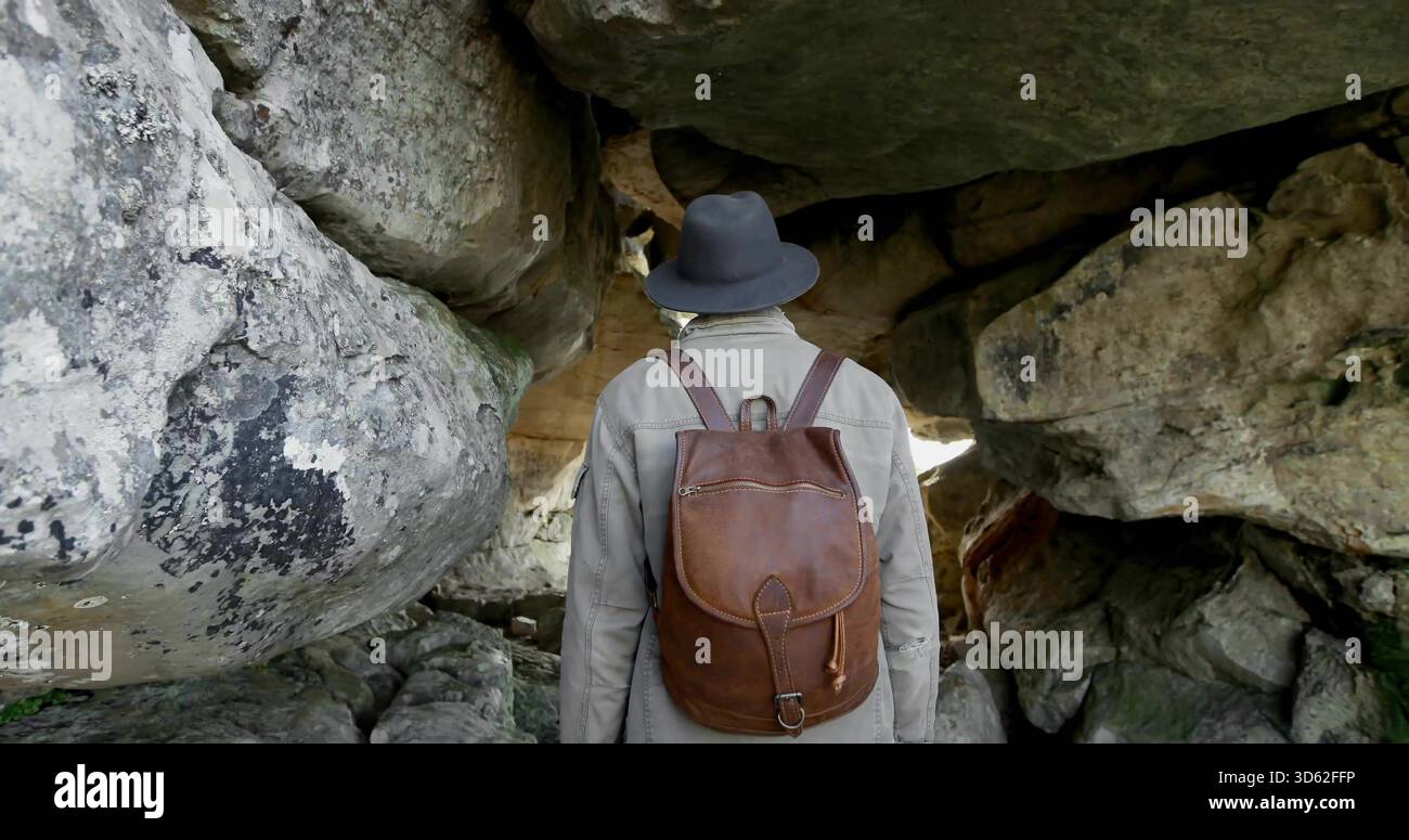 Standing hiker peering into crevice beneath overhang, wearing light ...