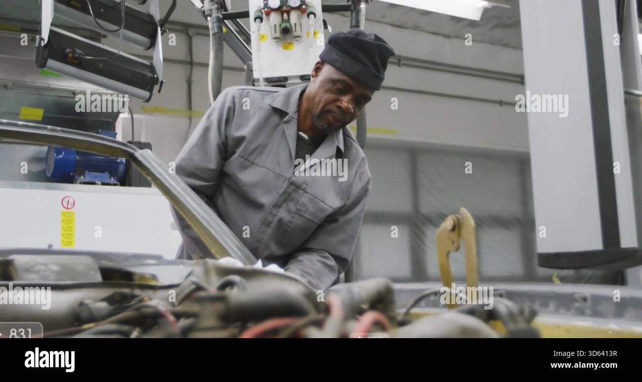 Leaning mechanic in grey coveralls and dark cap checking engine at ...