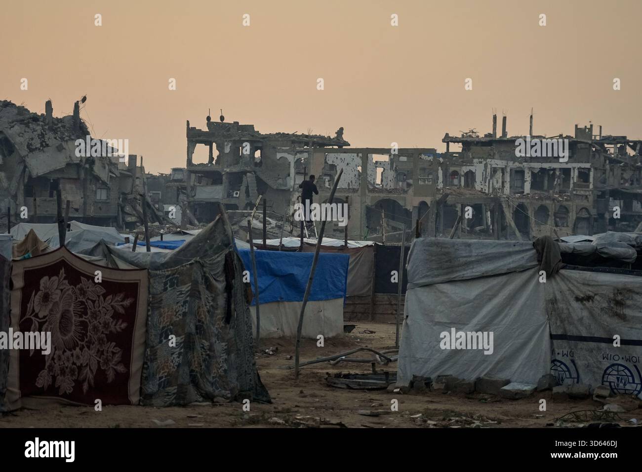 A man climbs a ladder as he repairs his tent in the Al-Shati camp in ...