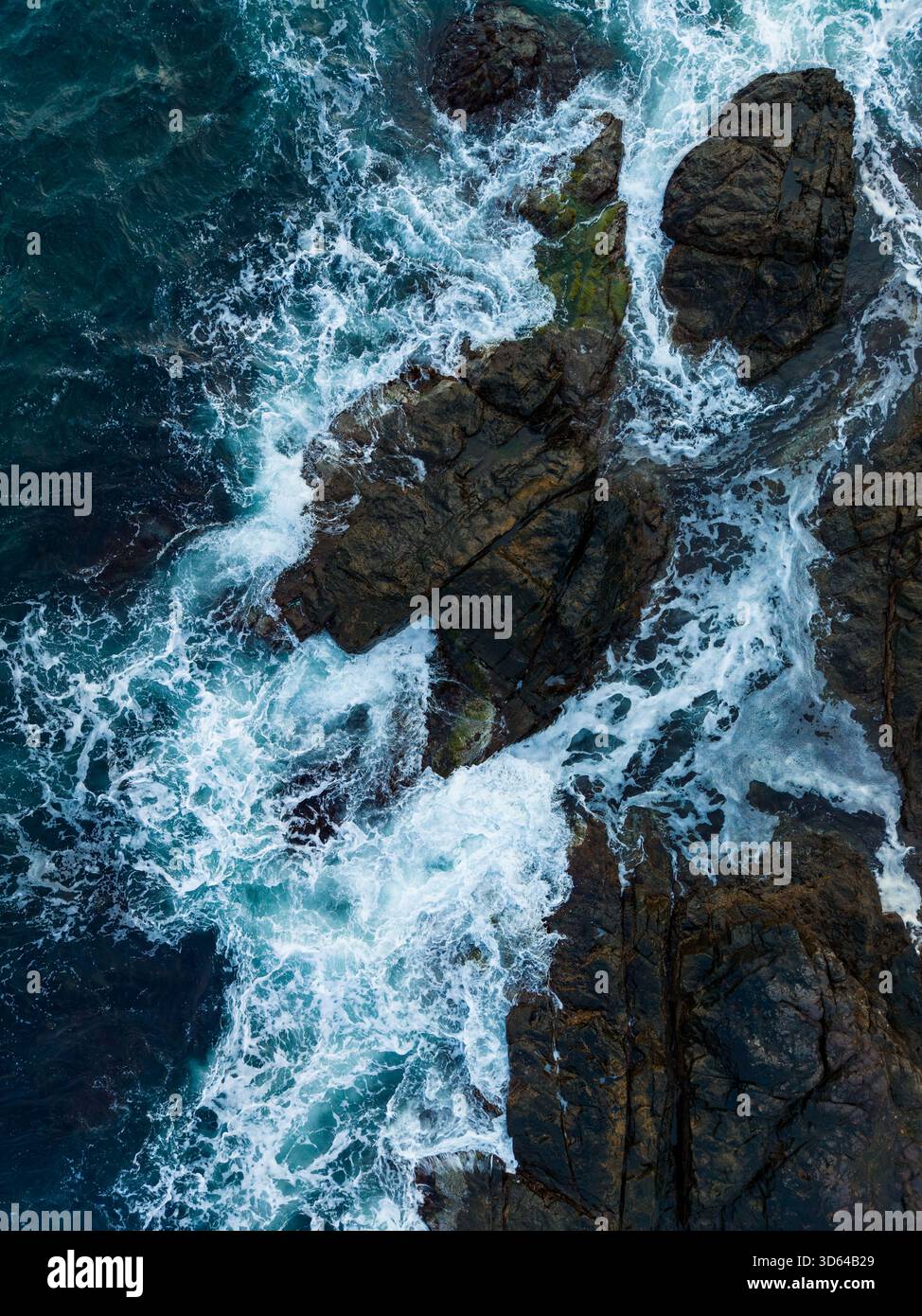 Powerful waves surge and crash against dark, jagged rocks at a ...