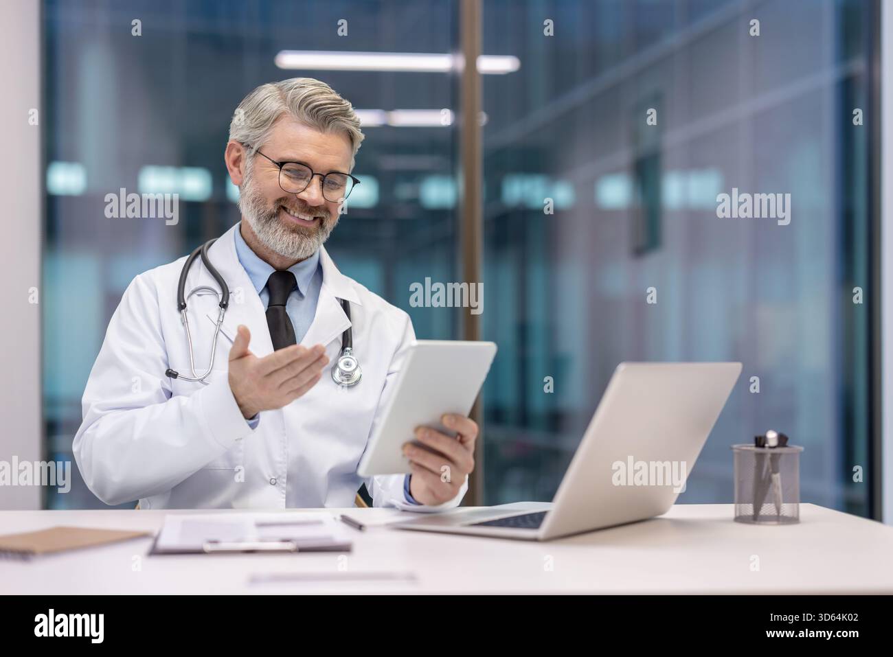 Male doctor in white coat and stethoscope smiles during a telemedicine ...