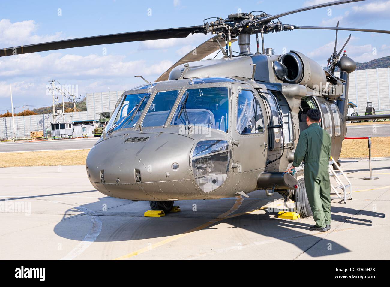 A military utility helicopter parked on an airfield with a crew member ...