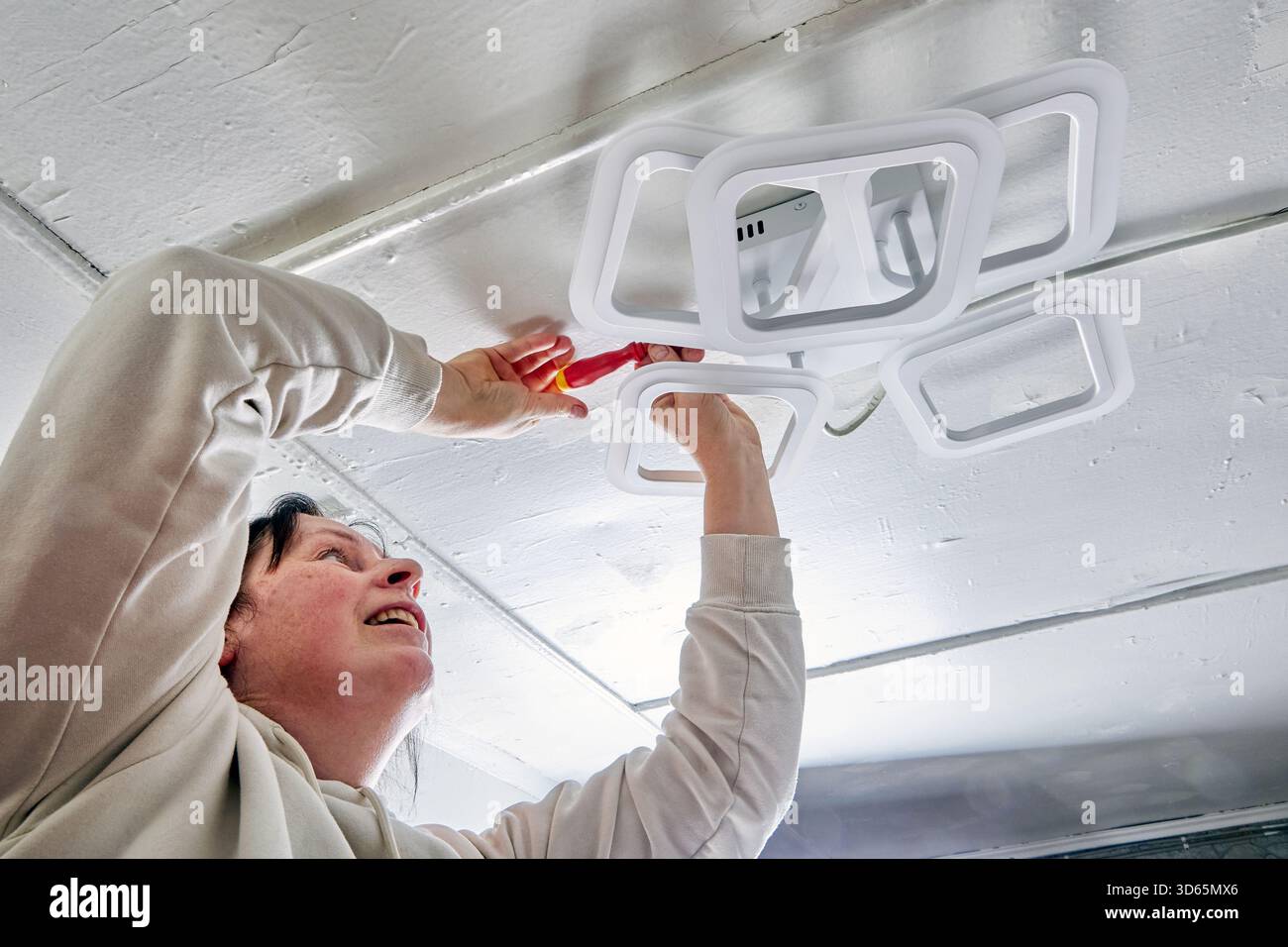 Securing lighting fixture on ceiling is executed by woman technician ...